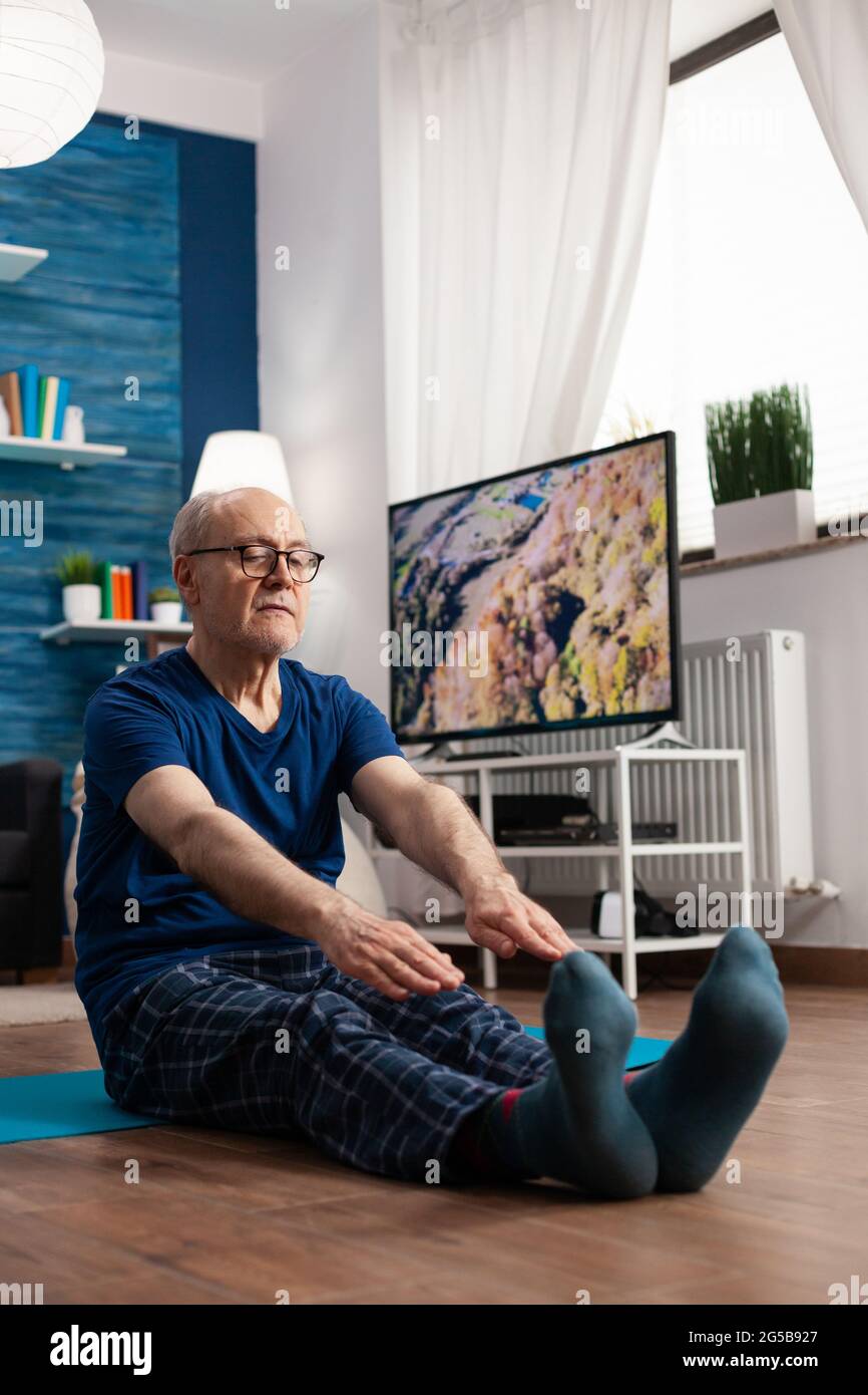 Retirement senior man sitting on yoga mat stretching legs muscles ...