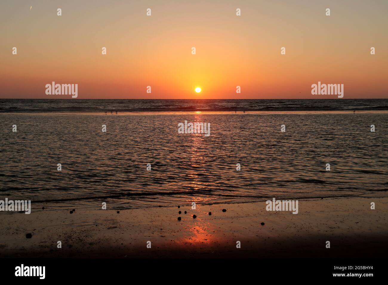 sun sinks into the sea on the beach of Katwijk with colorful sky in the ...