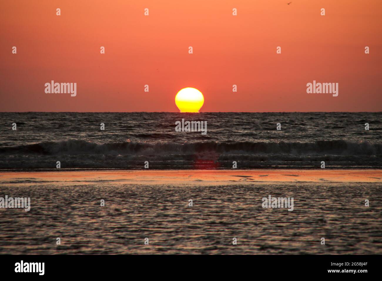 sun sinks into the sea on the beach of Katwijk with colorful sky in the ...