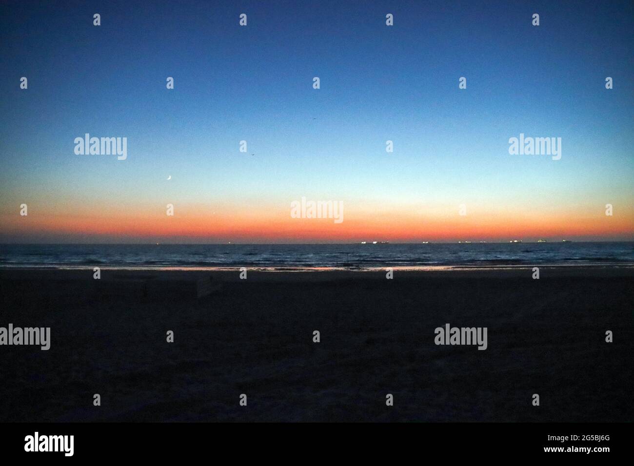 sun sinks into the sea on the beach of Katwijk with colorful sky in the ...