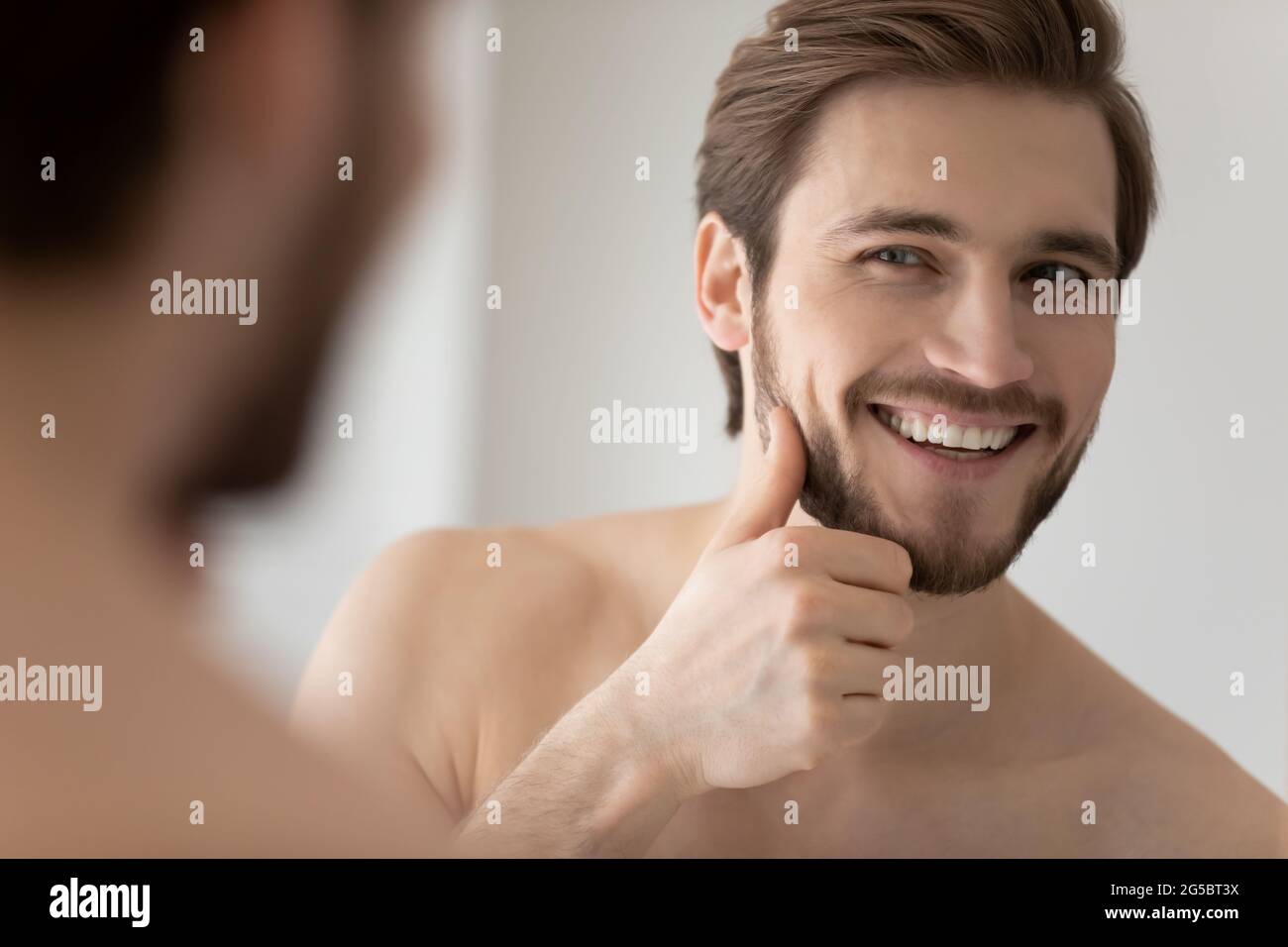 Happy millennial young handsome man looking in mirror in bathroom Stock ...