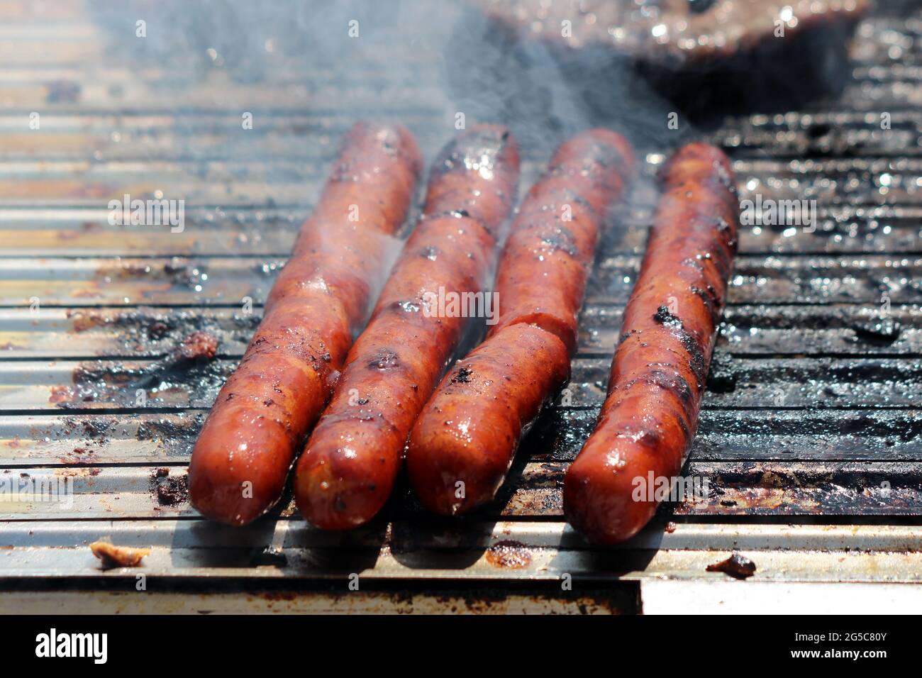 Four well done sausages grilling on the outside charcoal barbeque grill ...