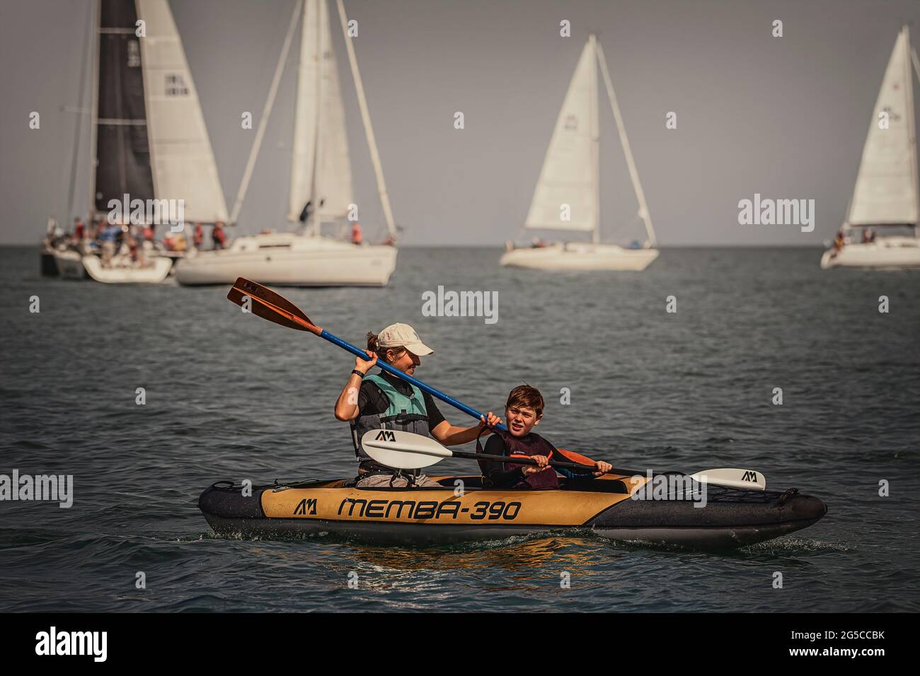 Kayakers in front of sailing boats. Lady instructor training boy Stock ...
