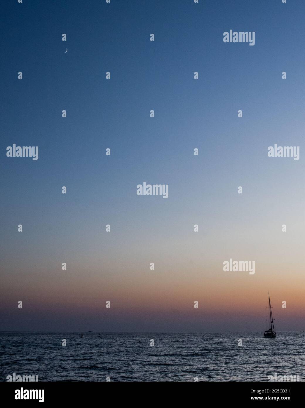 Boat sailing into the horizon during sunset with a small moon in the ...