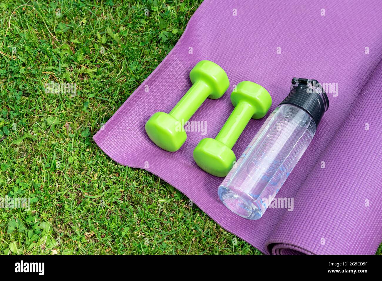 Ladie's dumbbells, fitness mat and sneakers on the green grass ...