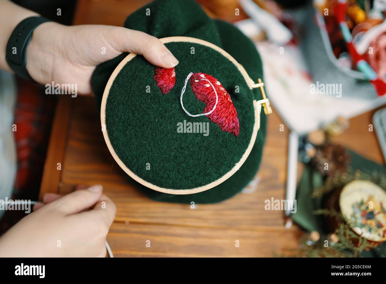 Girl's hands embroidery fly agaric hat on frame. Wooden table with ...