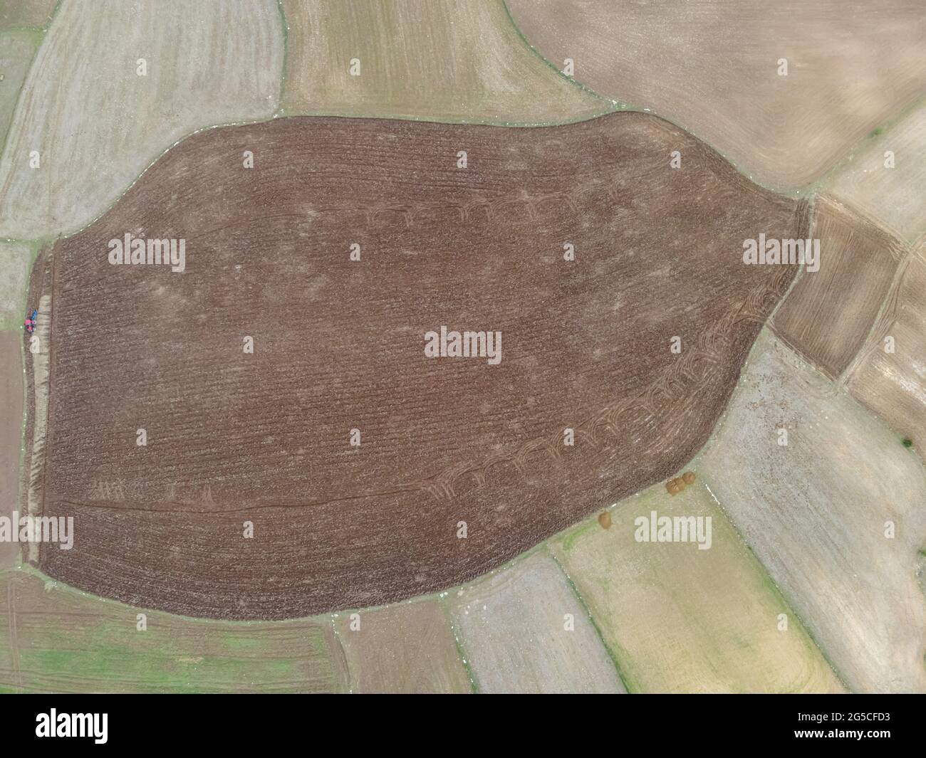 Aerial view of a tiny tractor plowing the huge field in the spring ...