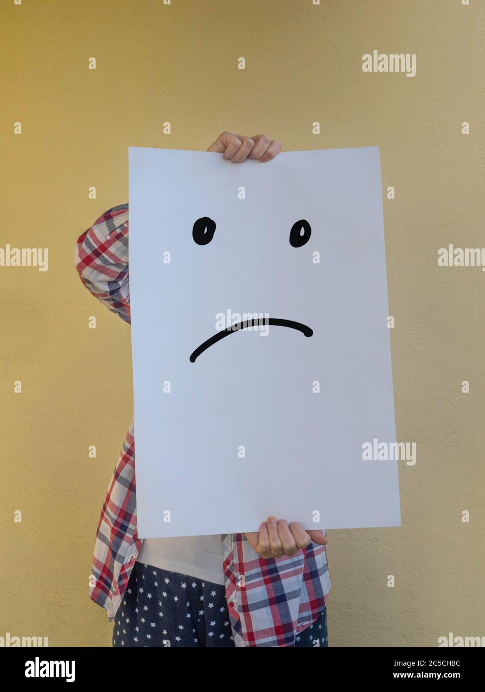 Casual woman hiding her face behind a blank billboard with a sad face ...