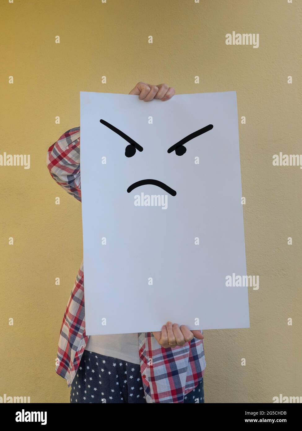 Casual woman hiding her face behind a blank billboard with an angry ...