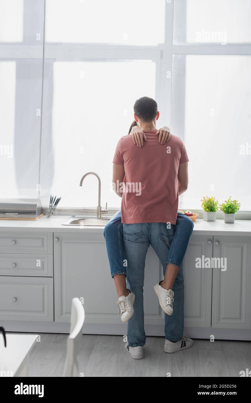 back view of young man hugging girlfriend sitting on cupboard in ...