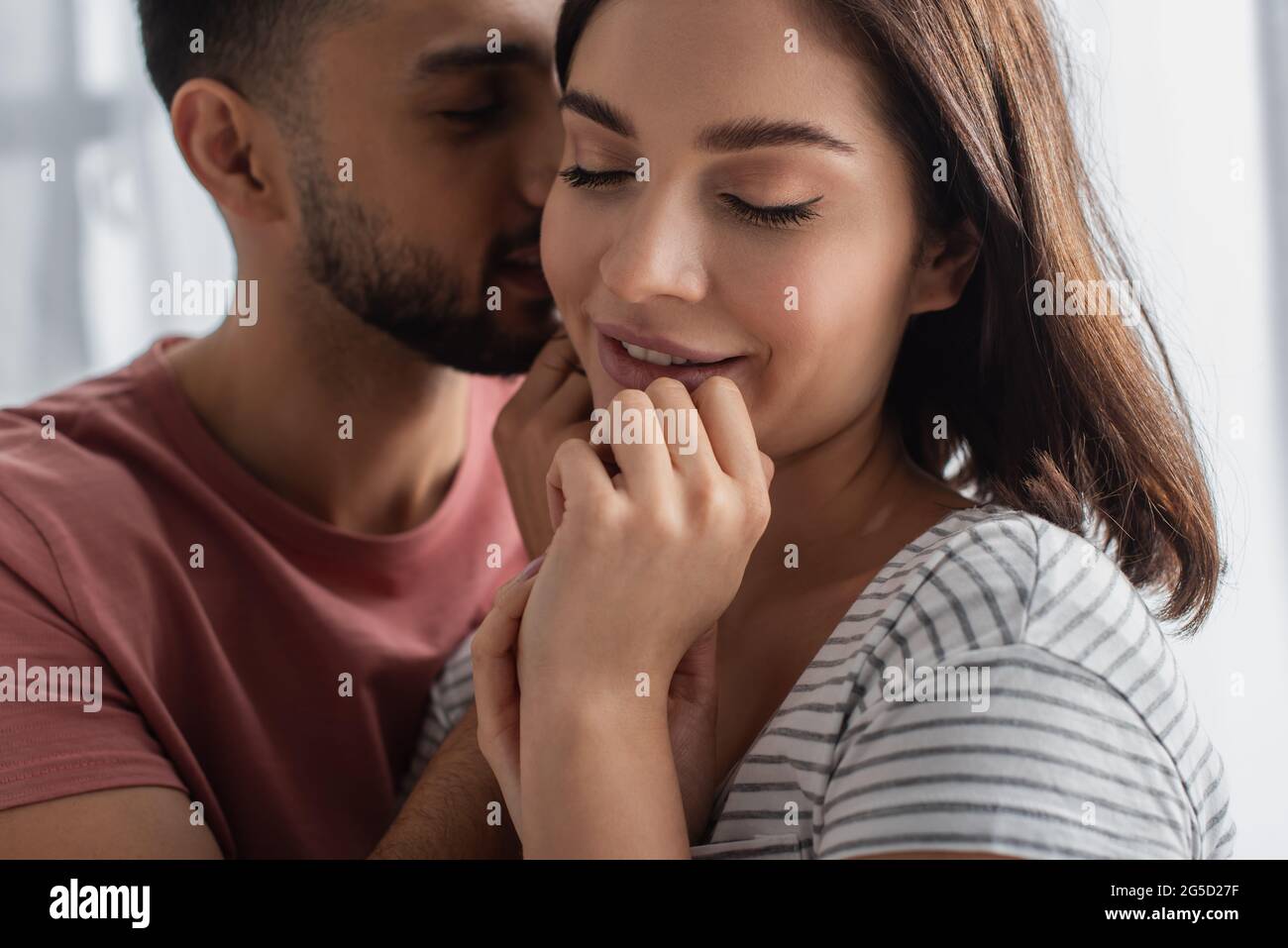 young man kissing smiling girlfriend with closed eyes and hands near ...