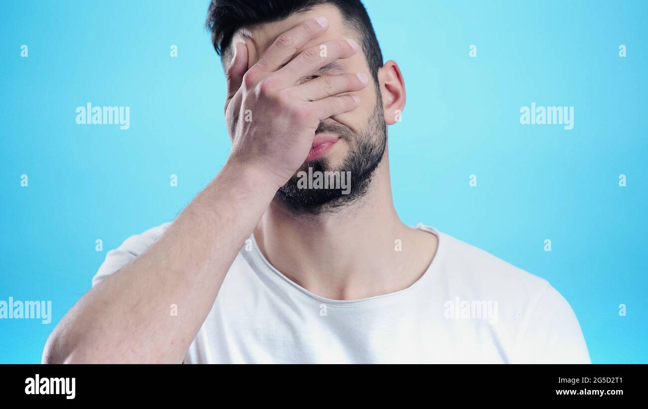 frustrated man obscuring face with hand isolated on blue Stock Photo ...
