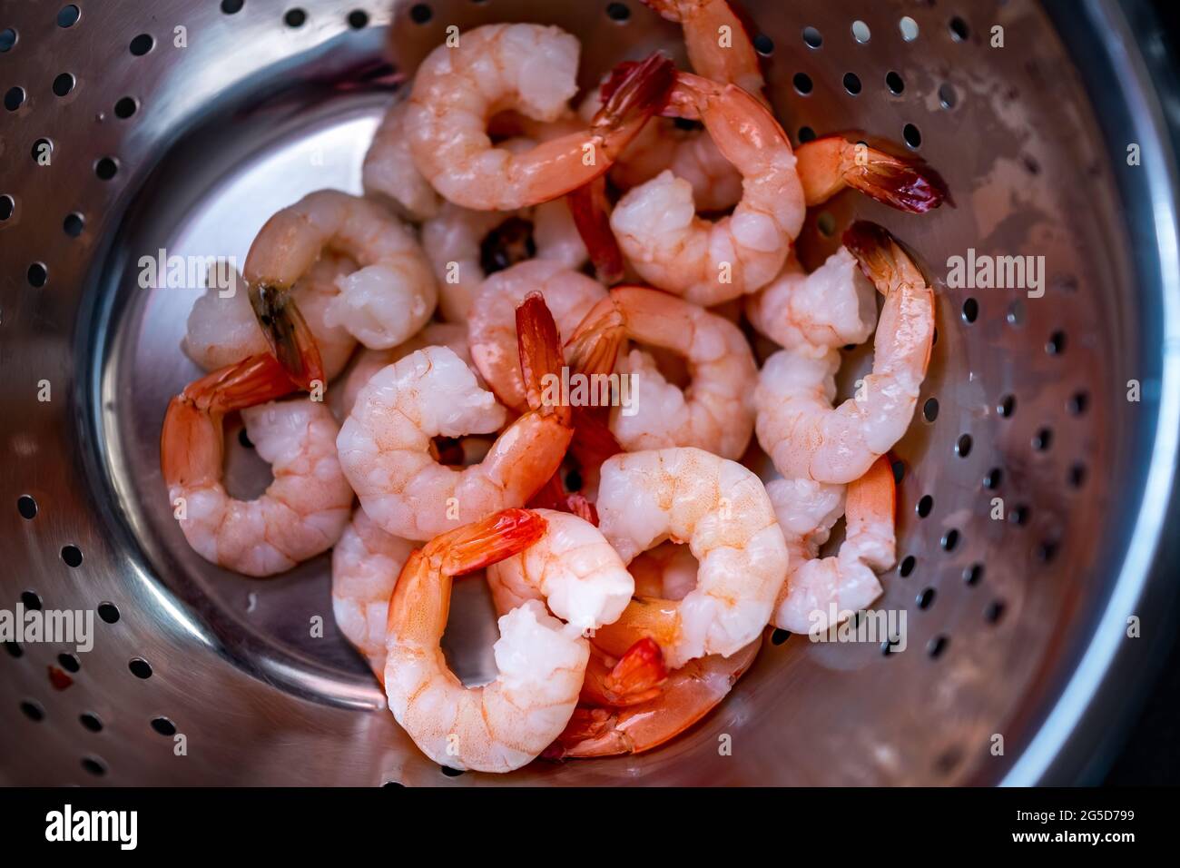 Close and selective focus on raw king prawns in a colander being ...