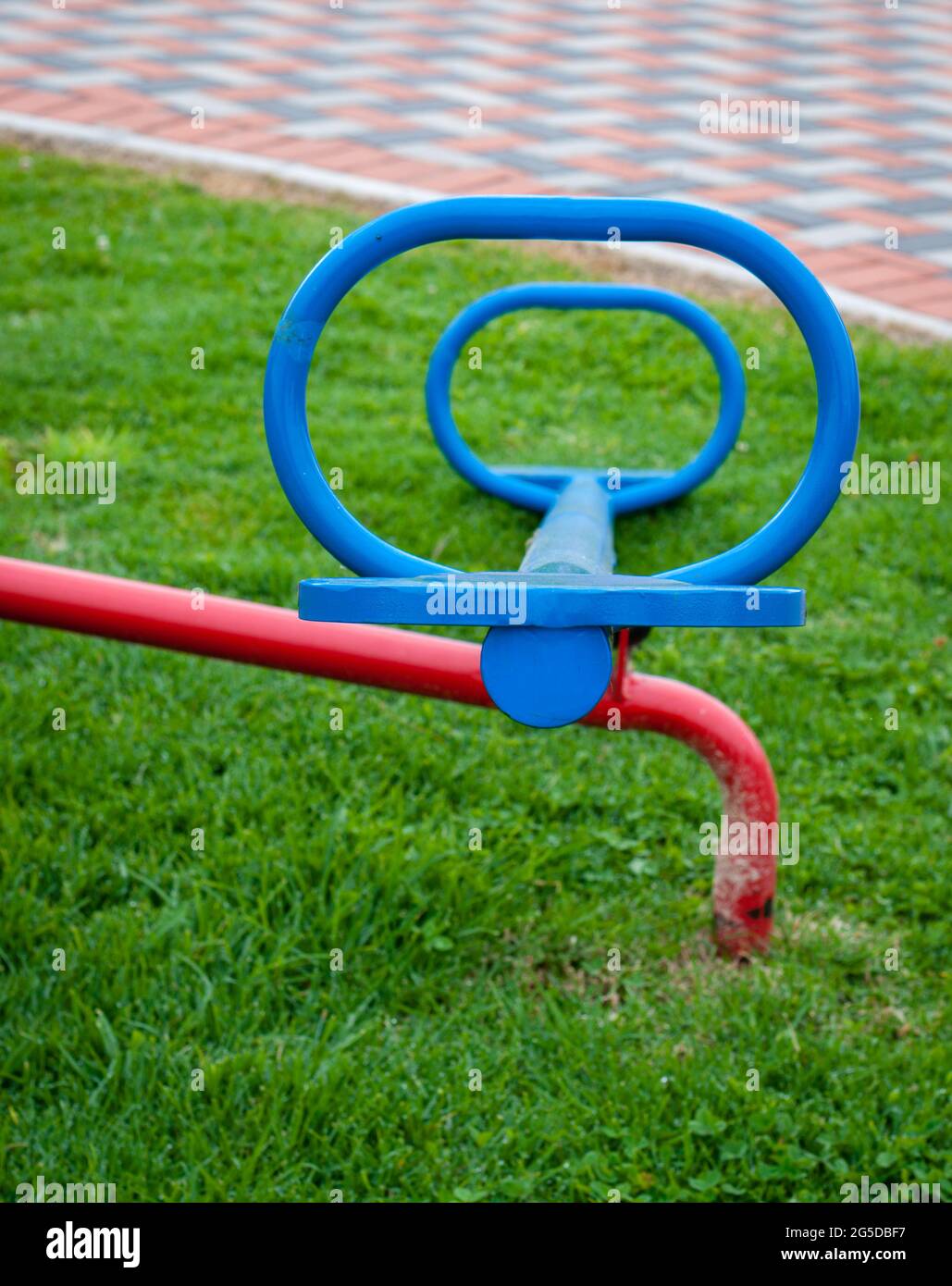 A red and blue teter toter on a grassy area of a children's playground ...