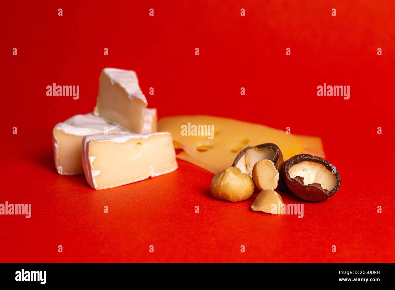 pieces of soft and hard cheese with nuts on a red background Stock ...
