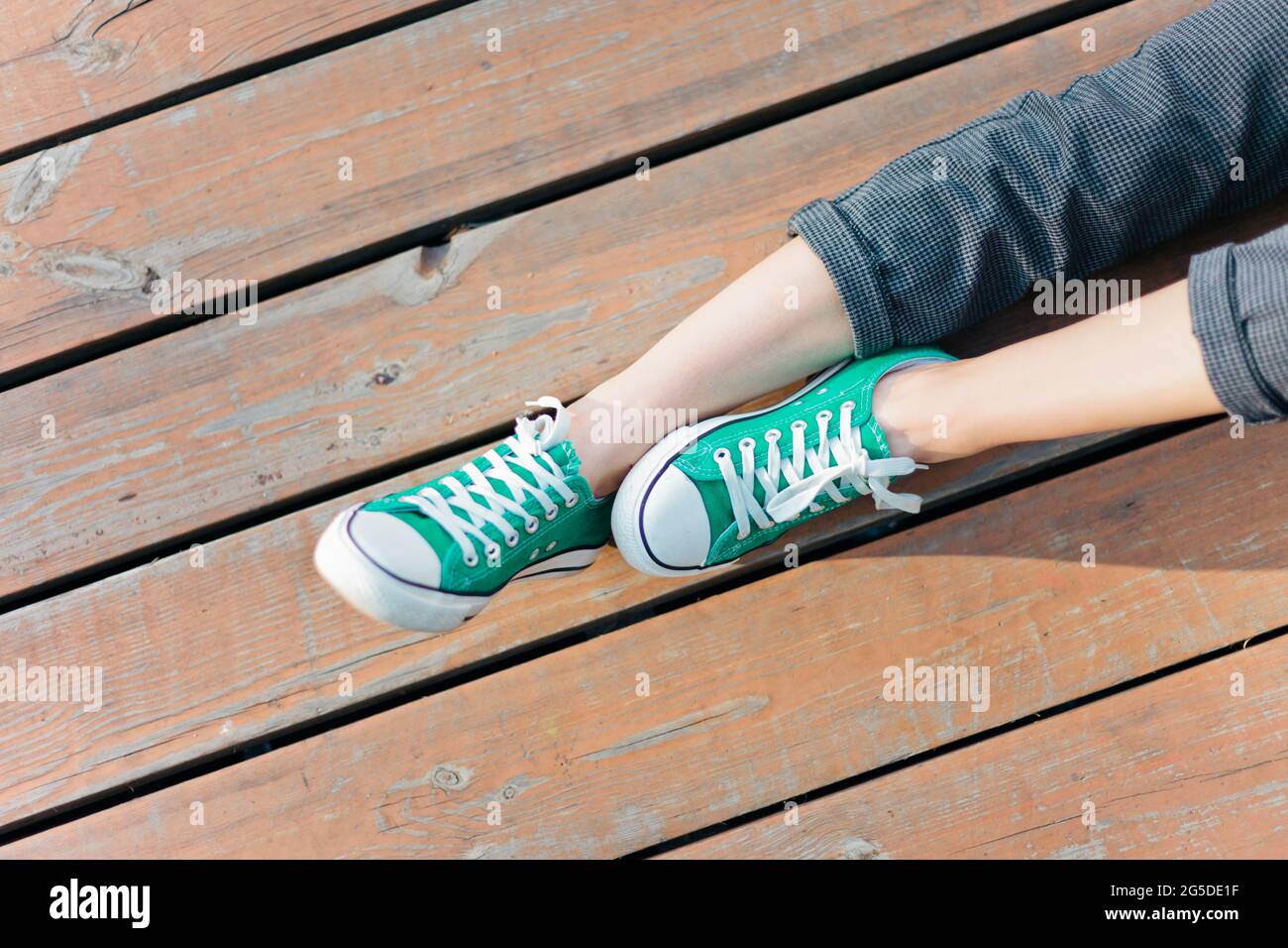Female legs in hipster sneakers on a wooden surface outdoors, crop ...