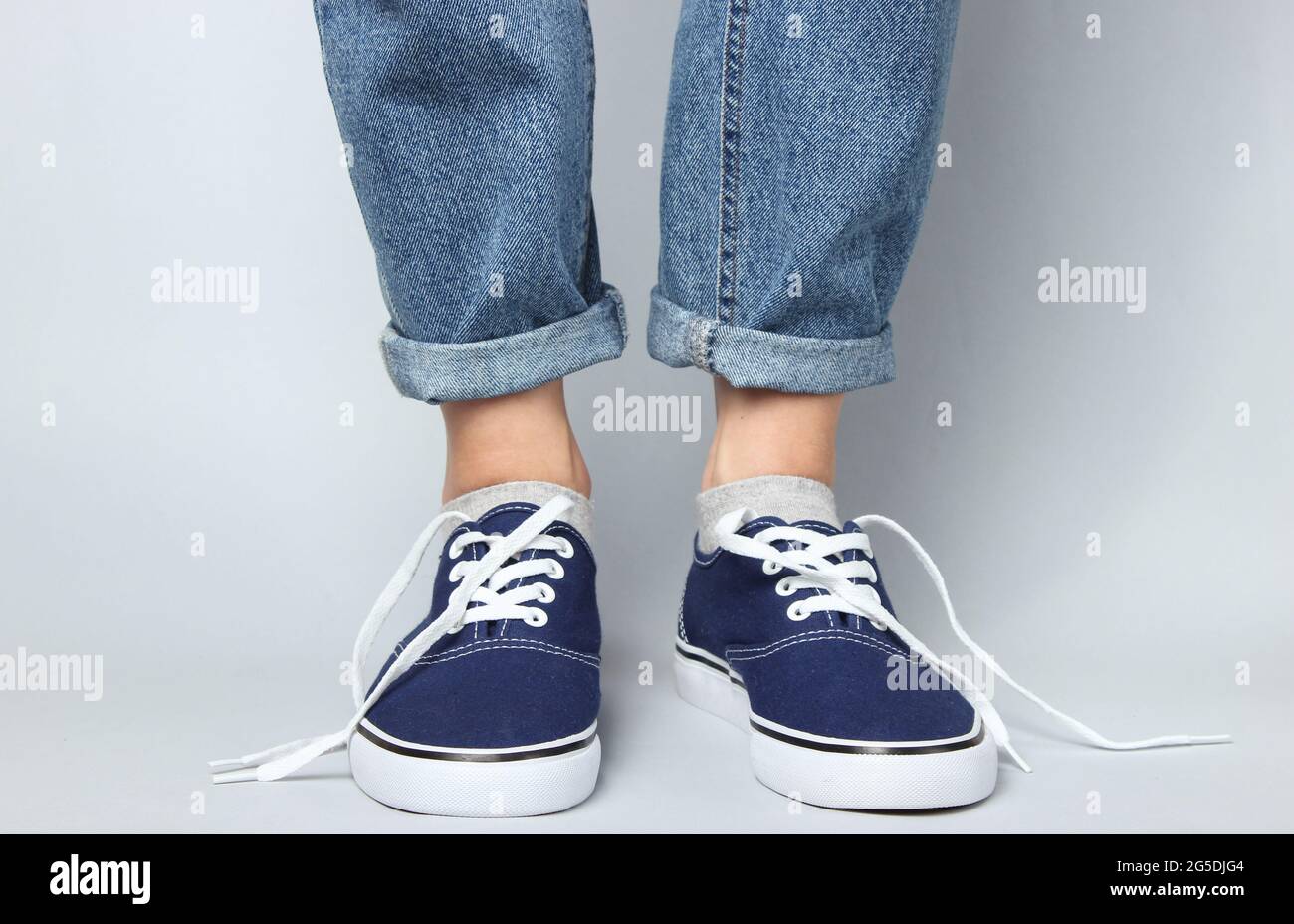 Fashion studio shot. Female legs in jeans and sneakers with untied ...