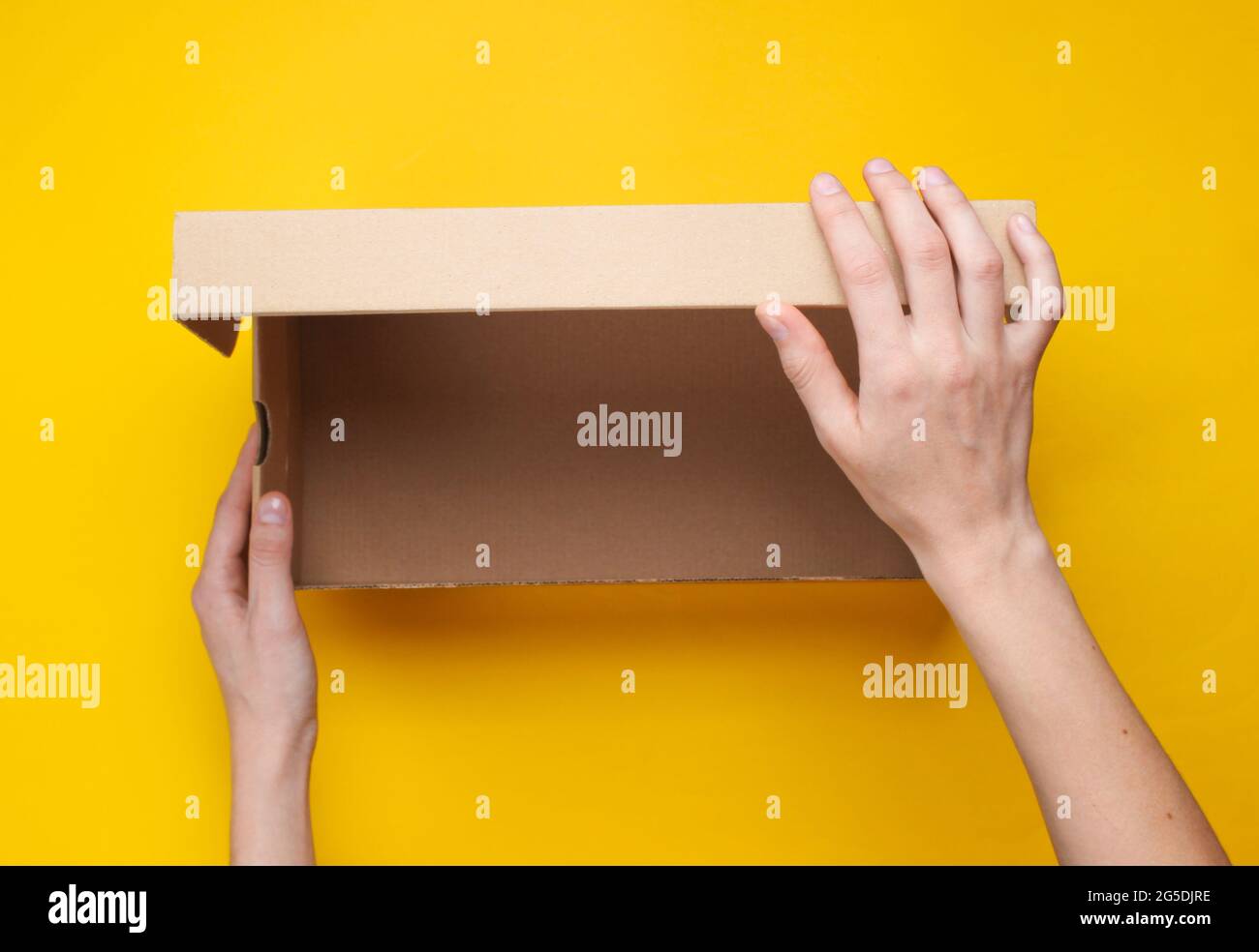 Female hands open empty cardboard box on yellow background. Top view ...