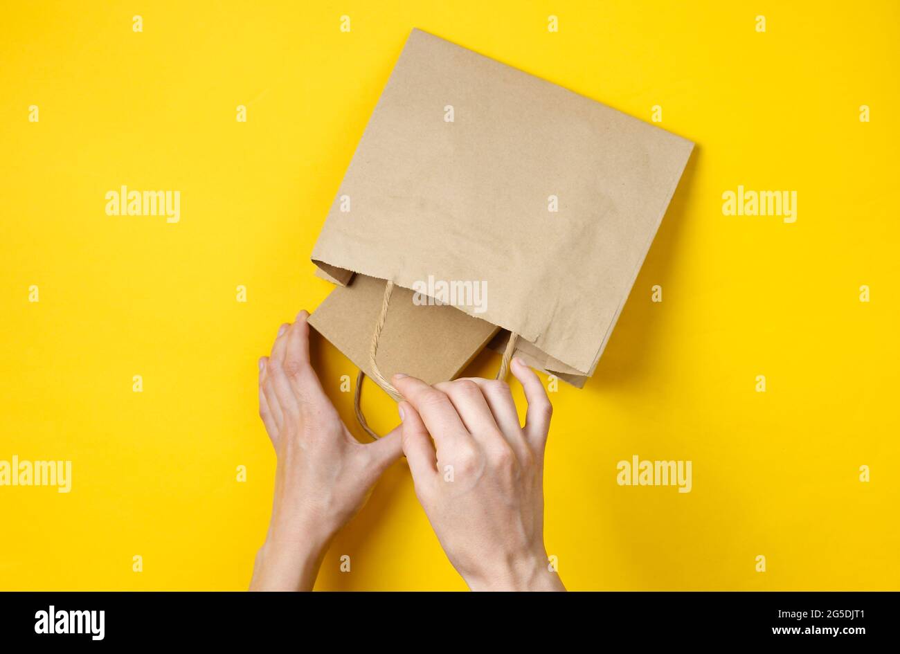 Female hands put a cardboard box in a paper bag on a yellow background ...