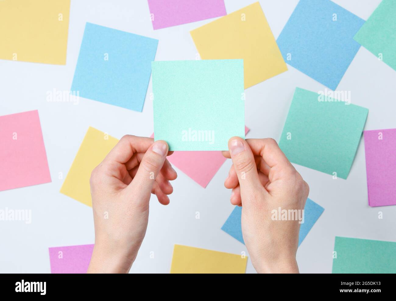 Female hand holding blue memo sheet of paper on a white background ...