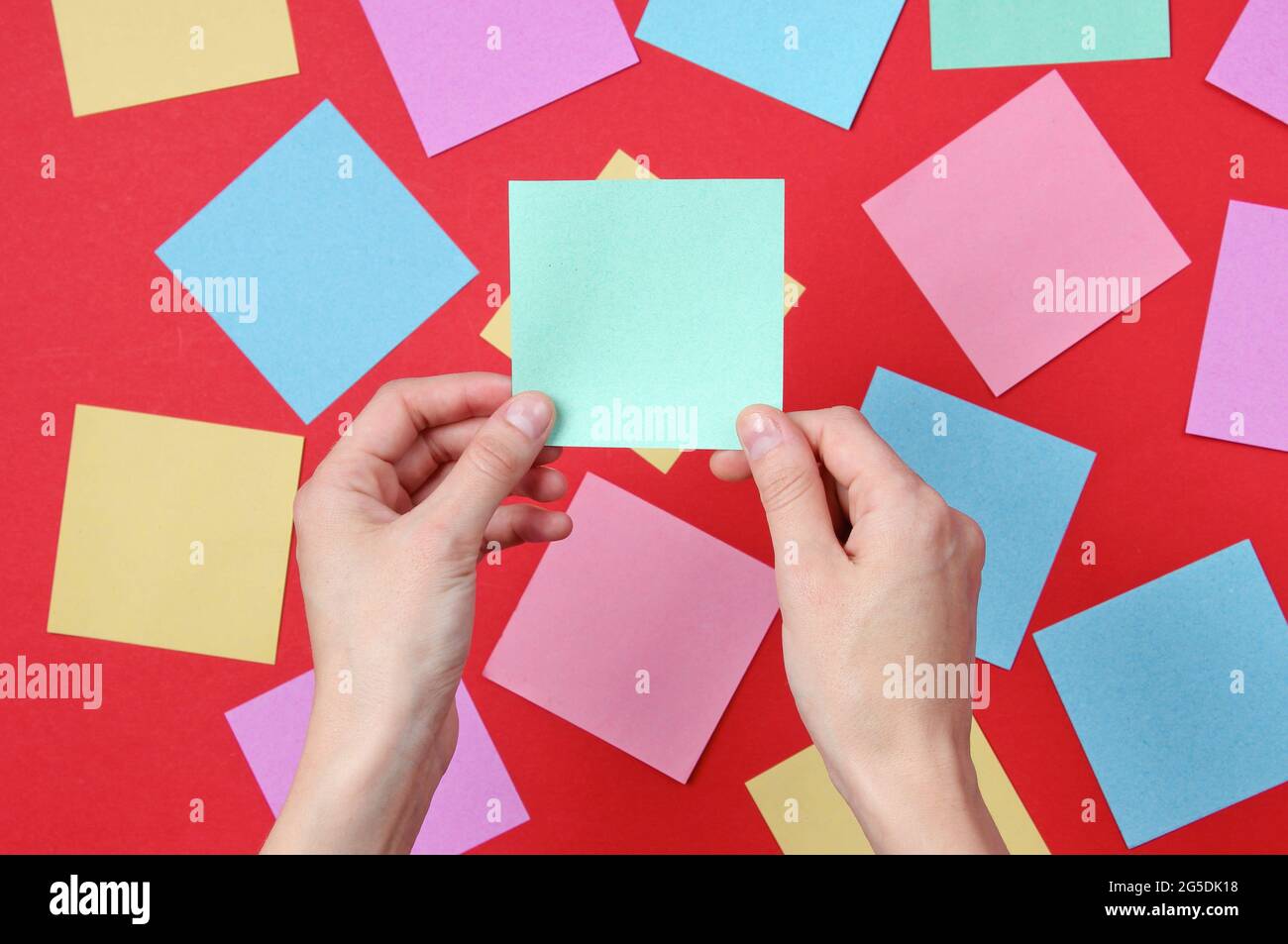Female hand holding blue memo sheet of paper on red background among ...