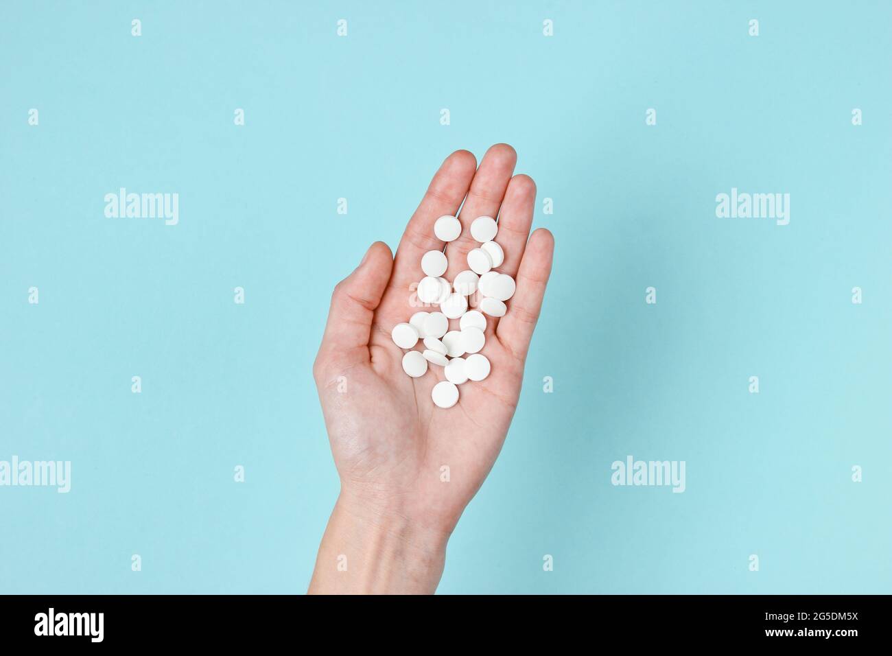 Many white tablets in the palm of hand on blue background. Medical ...