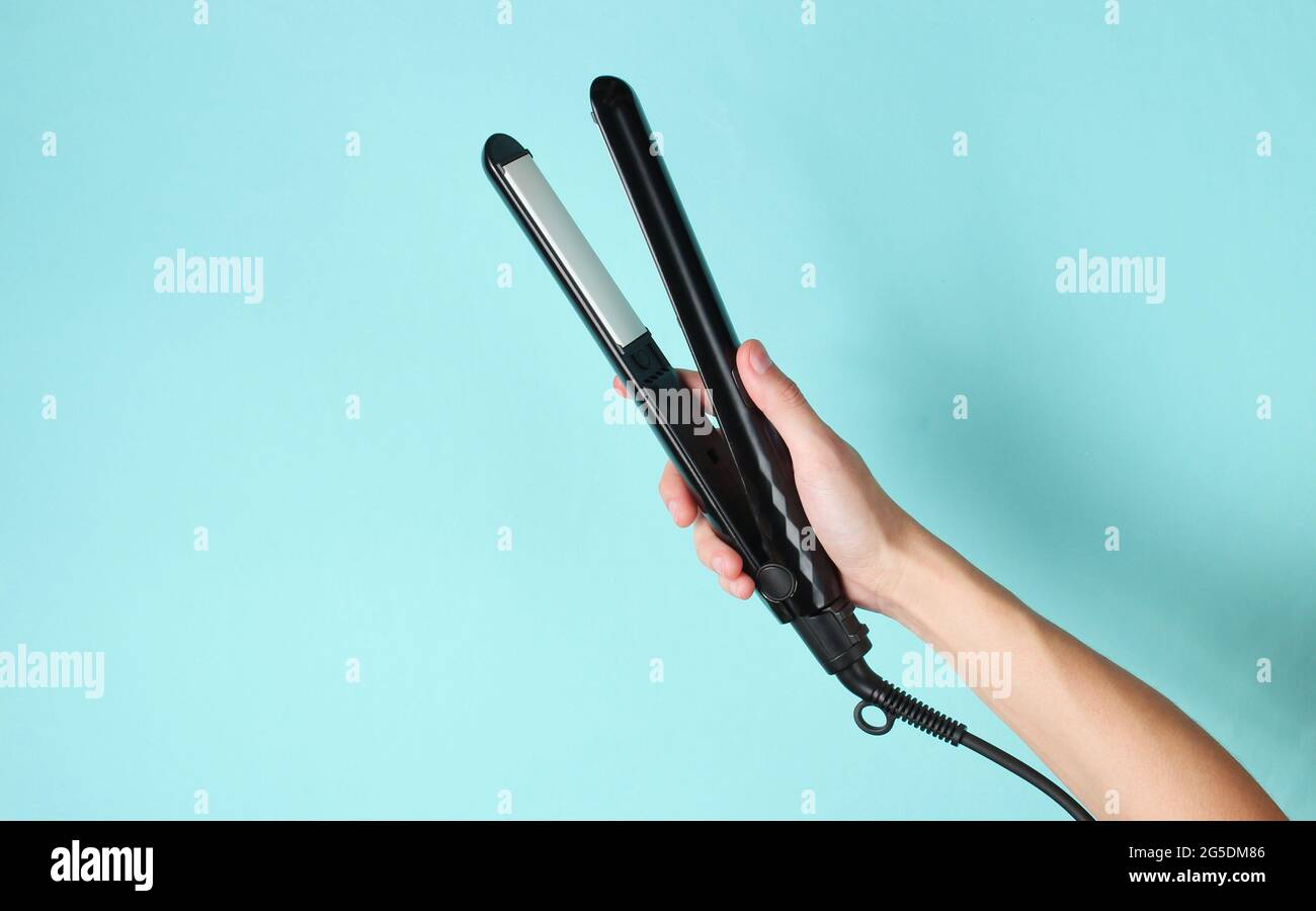 Hair care. Female hand holding hair straightener on blue background ...
