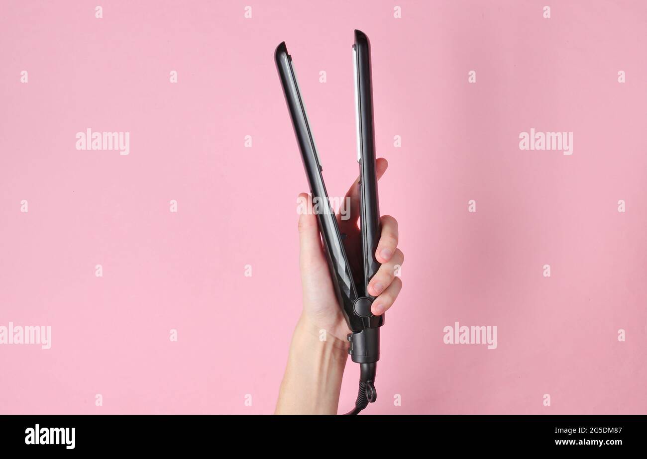 Hair care. Female hand holding hair straightener on pink background ...