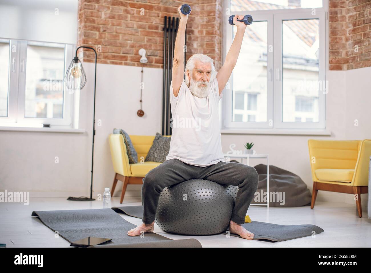 Mature man dressed in sport clothes using dumbbells and fitball for ...