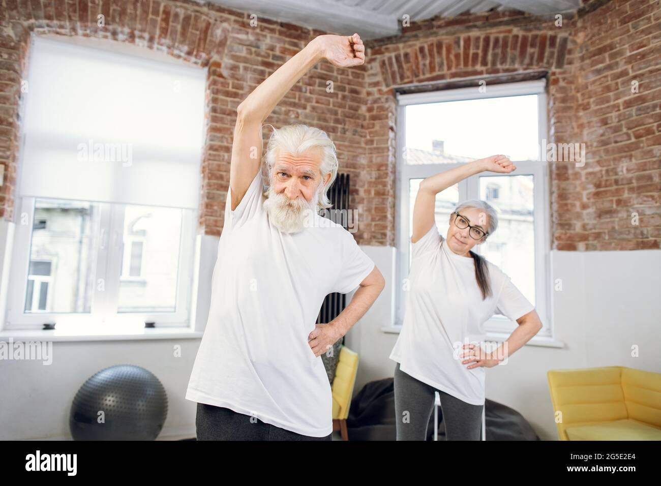 Two retired people on activewear doing sport exercises during morning ...