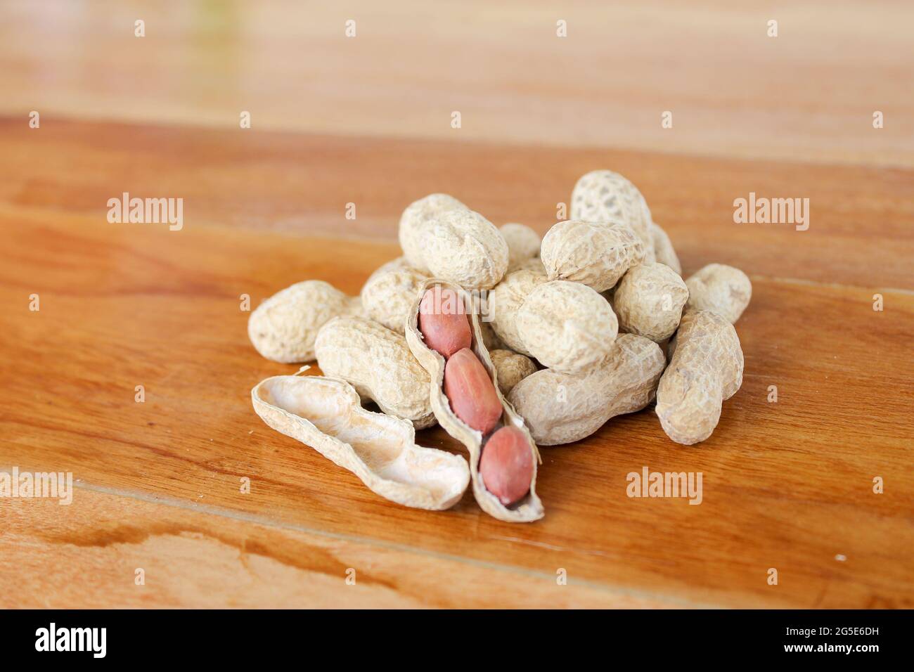 Peanuts on a wooden table. One peanut was peeled to reveal the red seed ...
