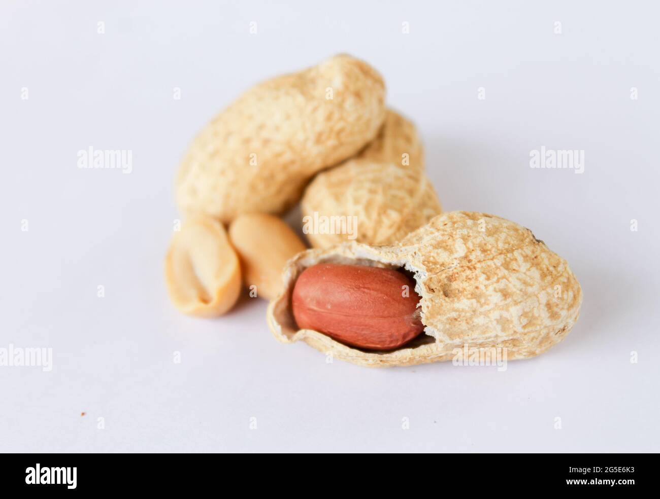 Peanuts are on a white background. One was peeled to reveal a red seed ...