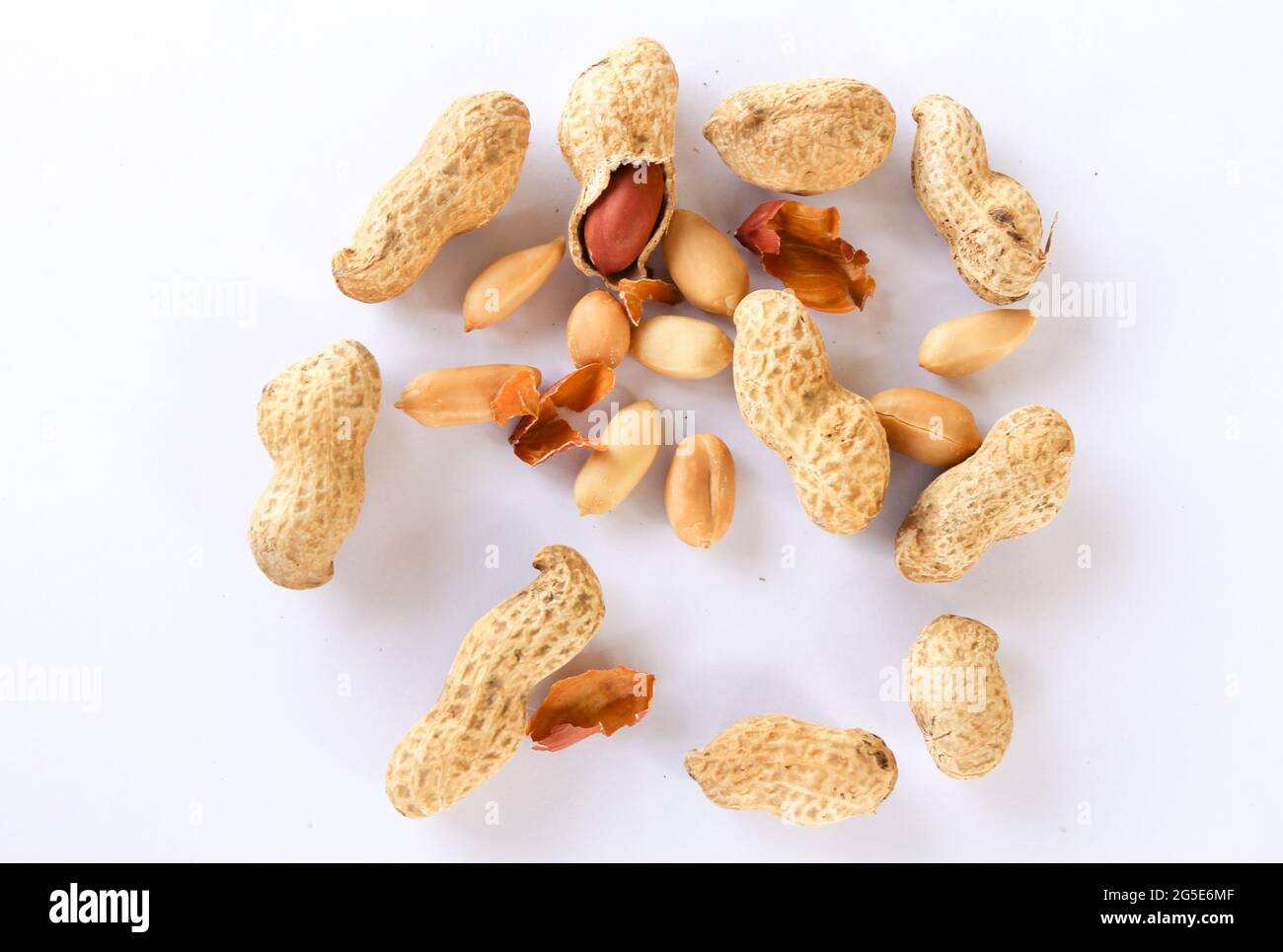 Peanuts are scattered on a white background, some are removed to reveal ...