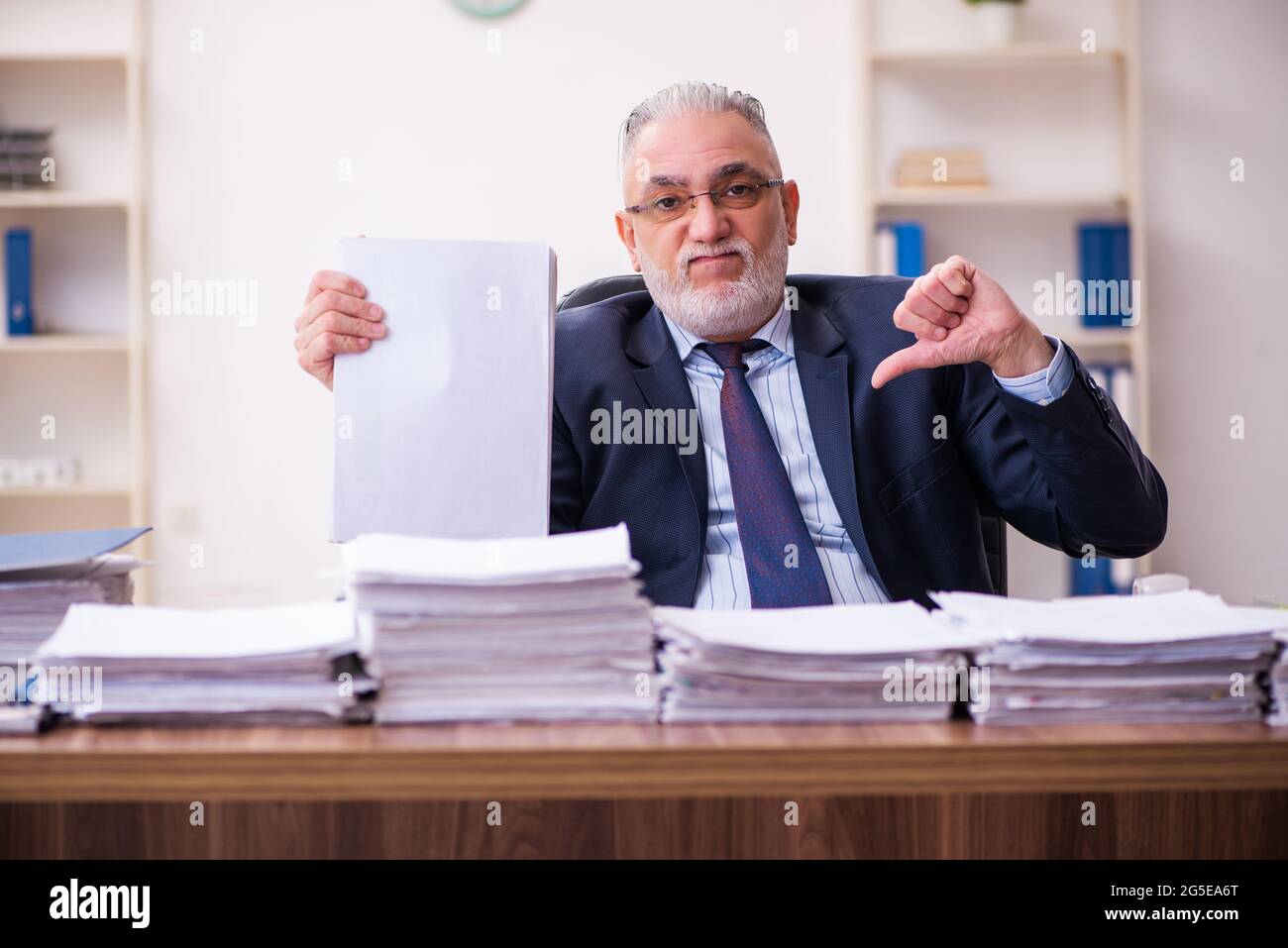 Old male employee unhappy with excessive work at workplace Stock Photo ...