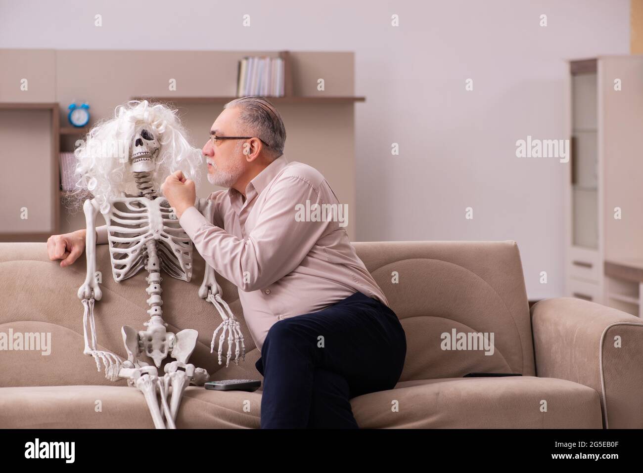 Old man sitting on the sofa with the female skeleton in undying love ...
