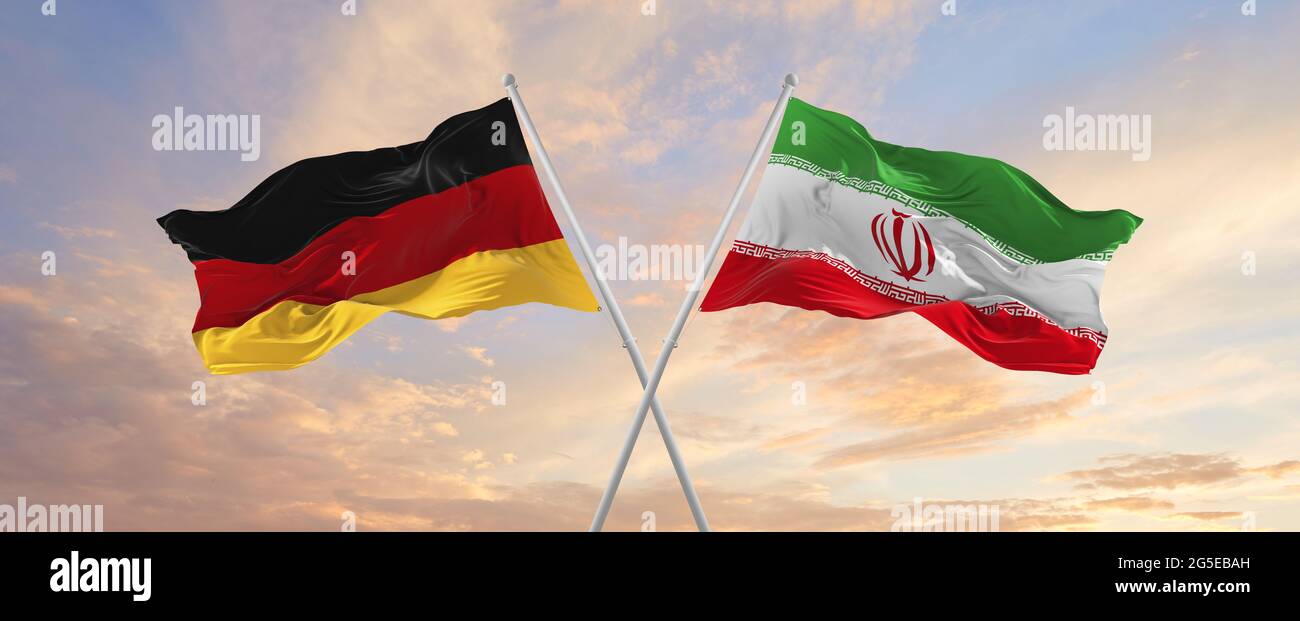 flags of Germany and Iran waving in the wind on flagpoles against sky ...