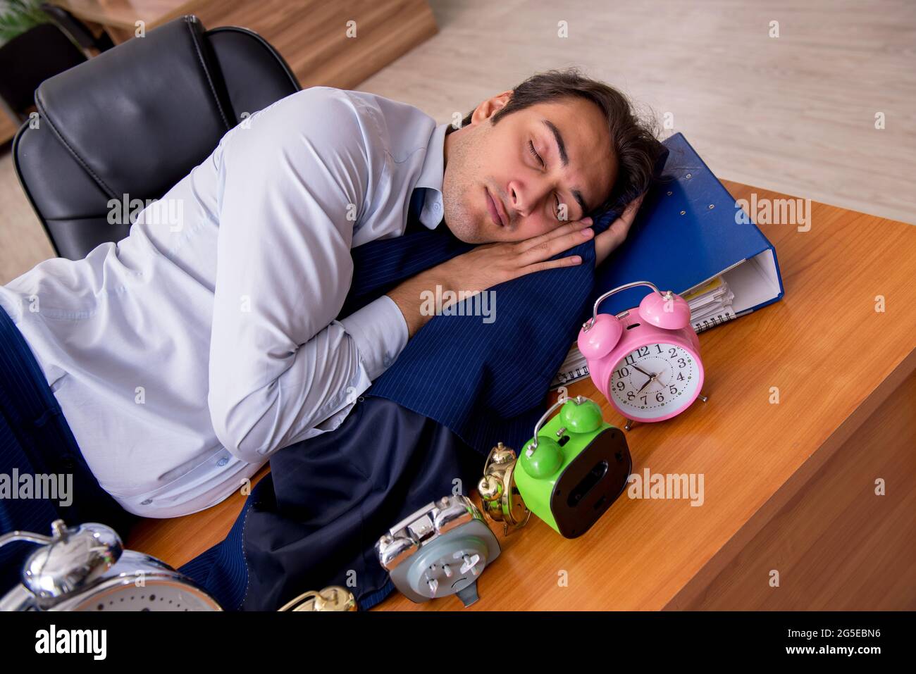 Young businessman sleeping in the office in time management concept ...