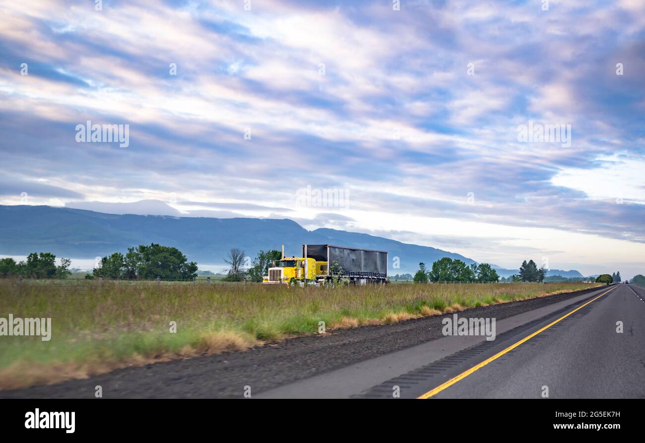 Yellow big rig long haul industrial semi truck with turned on headlight ...
