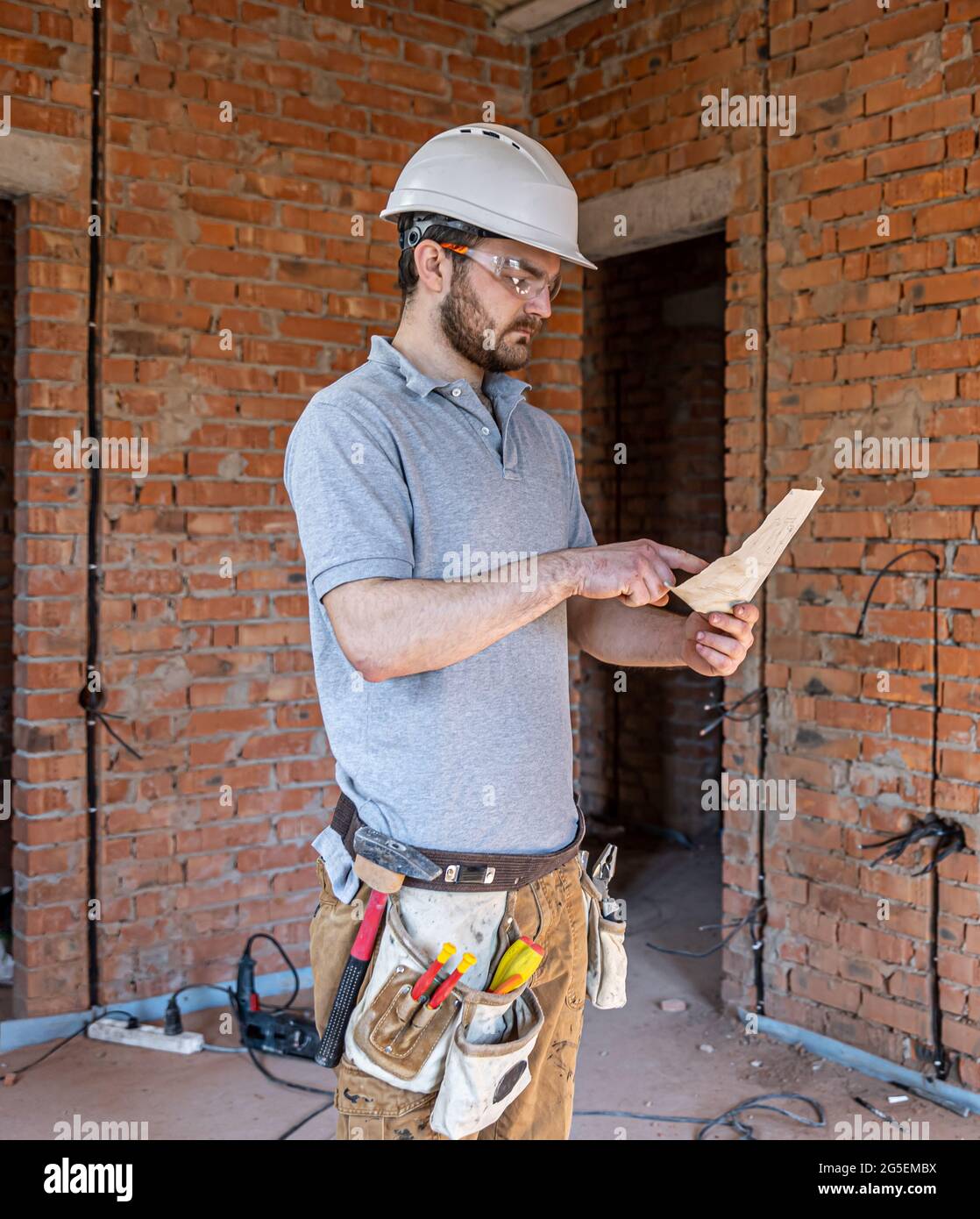A builder in work clothes examines a construction drawing at a ...