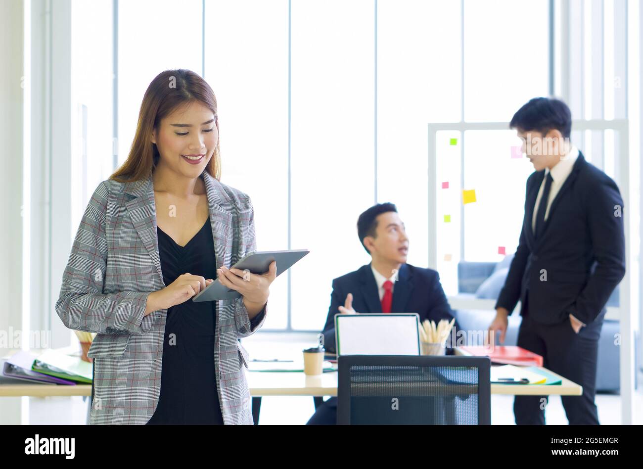 Young female employee in a plaid pattern suit standing with tablet ...