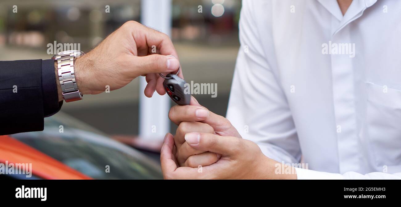 A businessman in black suit handling car key to the valet service staff ...