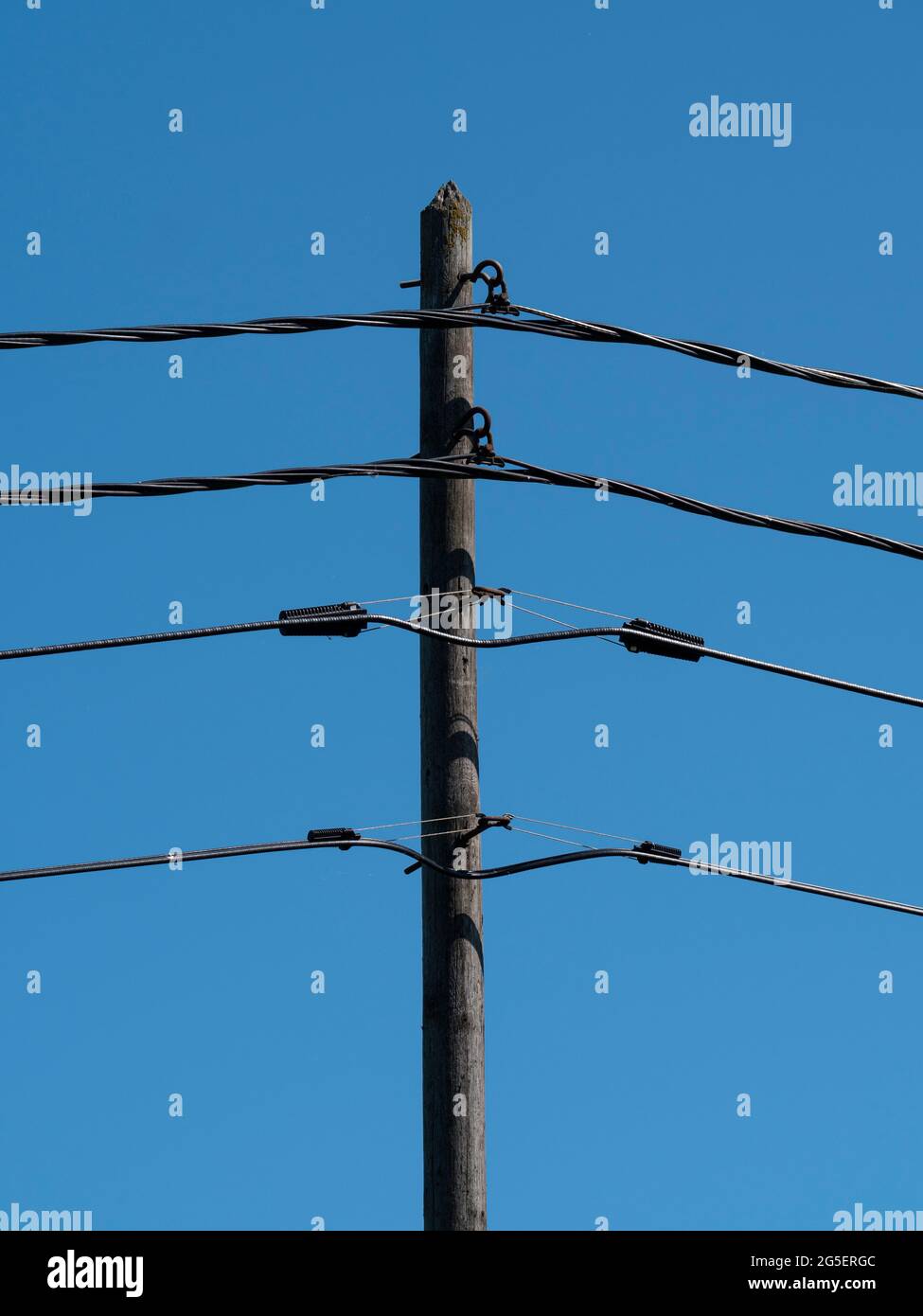 Wooden pole with seven electricity cables and a clear blue sky as ...