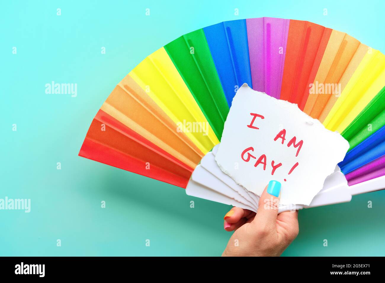 Text I am Gay on paper in hand with fake nails. Rainbow fan in colors ...