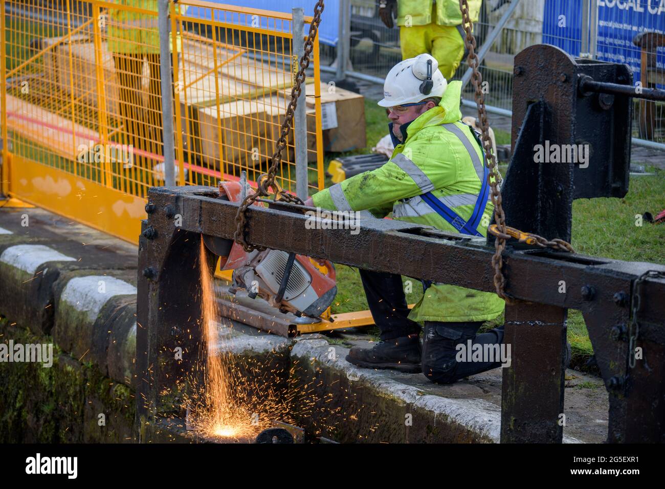 A male worker using a circular saw to cut through metal work whilst ...