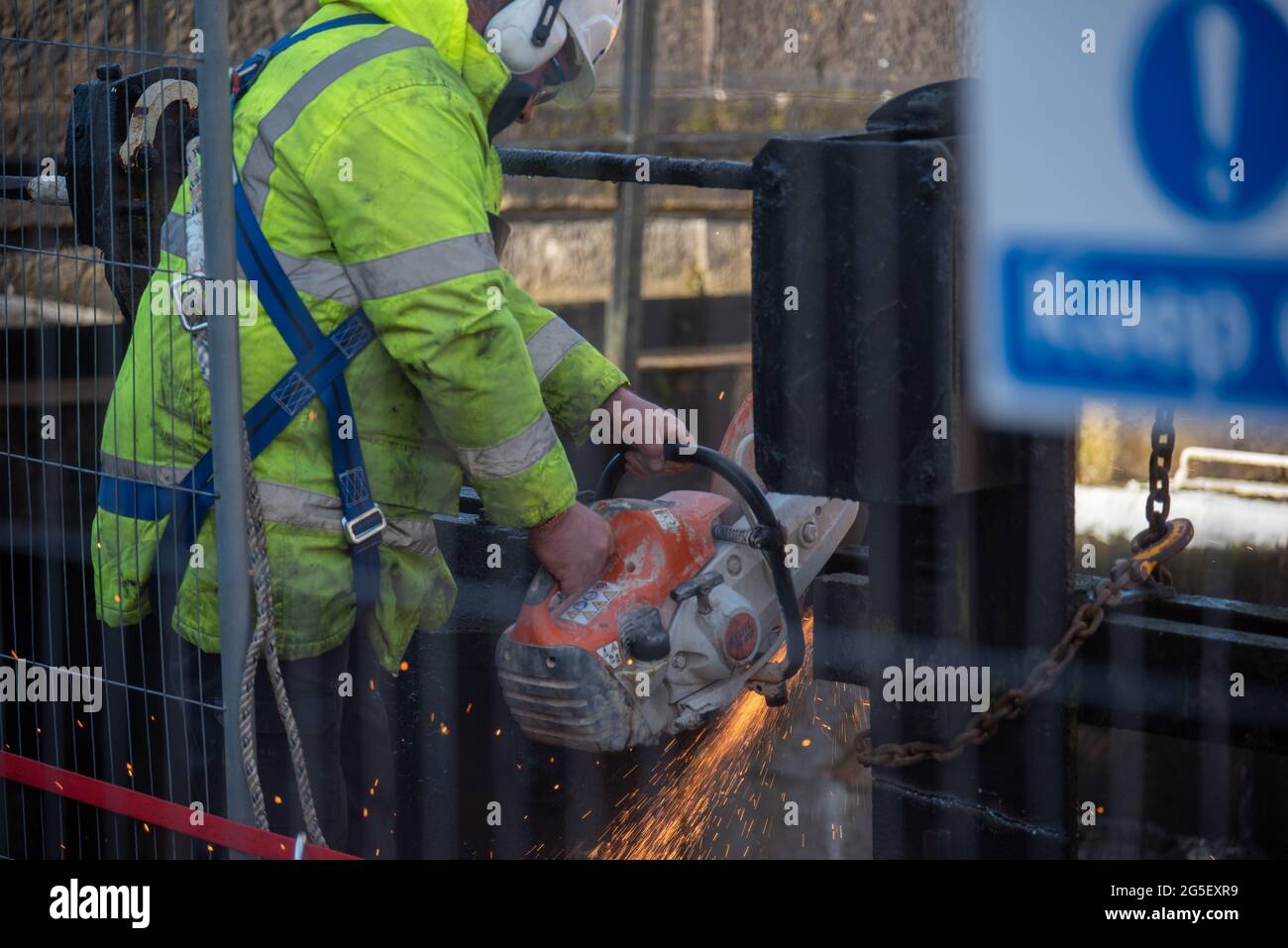 A male worker using a circular saw to cut through metal work whilst ...