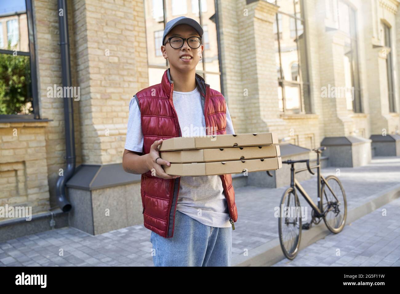 Young cheerful asian delivery boy holding boxes with pizza and l Stock ...
