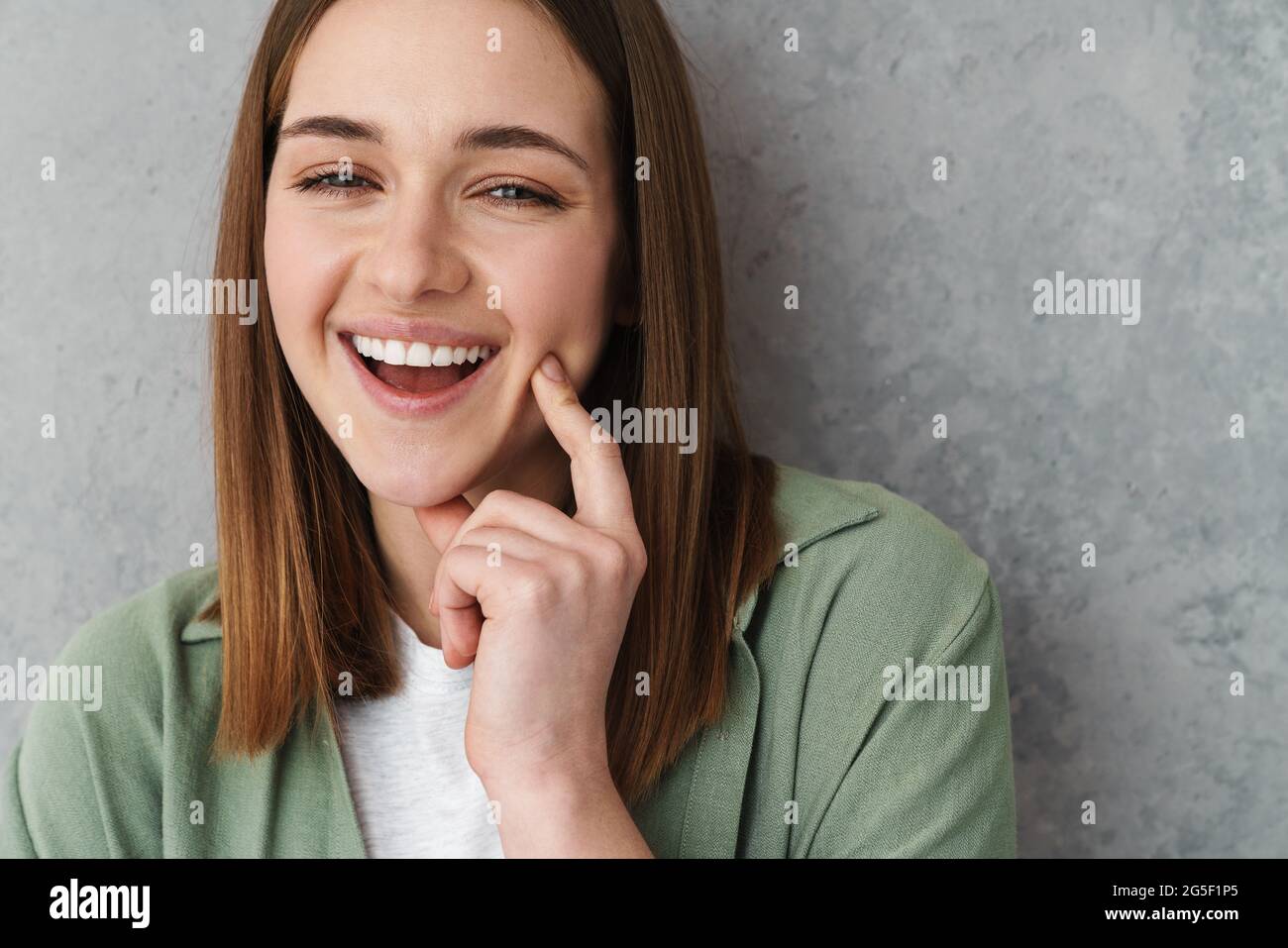 Happy beautiful nice girl smiling and pointing finger at her cheeks ...