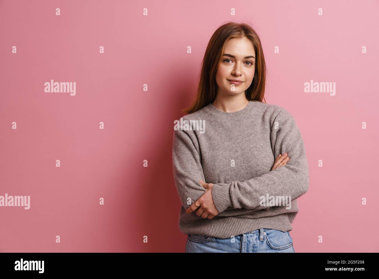 Young ginger pleased woman posing with arms crossed isolated over pink ...