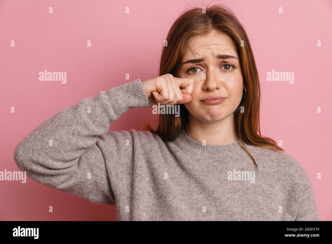 Young ginger upset woman crying and wiping her tears isolated over pink ...