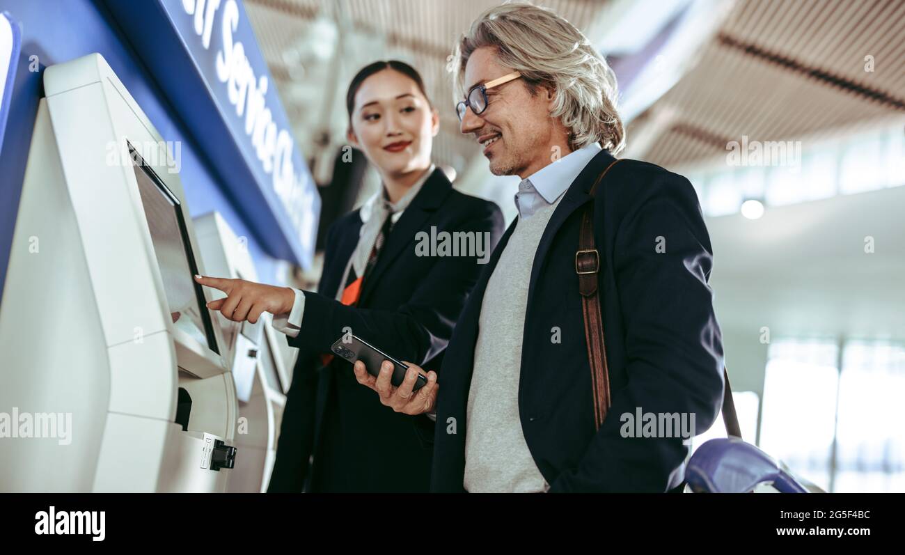 Female ground attendant helping male traveler with self check-in ...